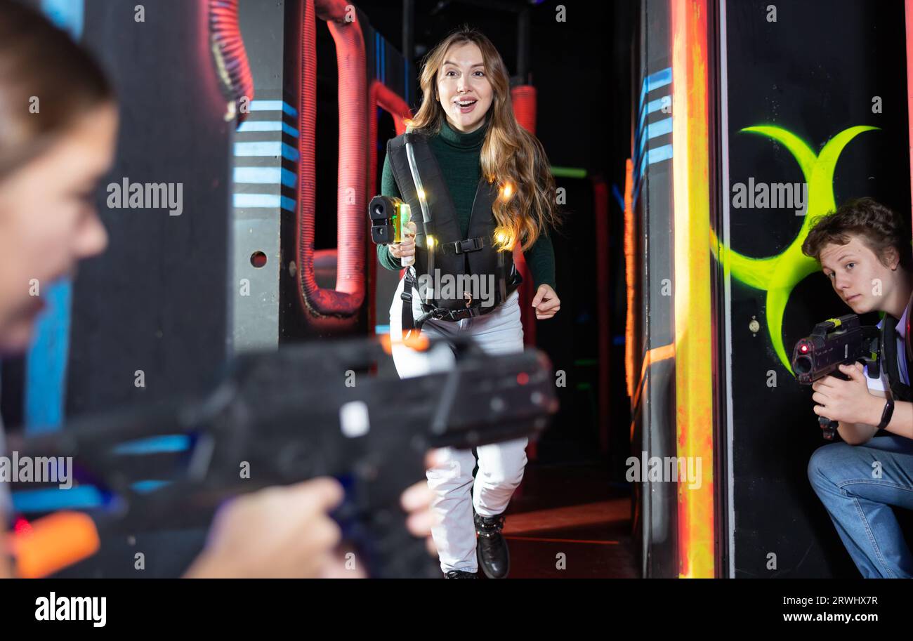 Joyous girl with laser pistol playing laser tag with friends on ...