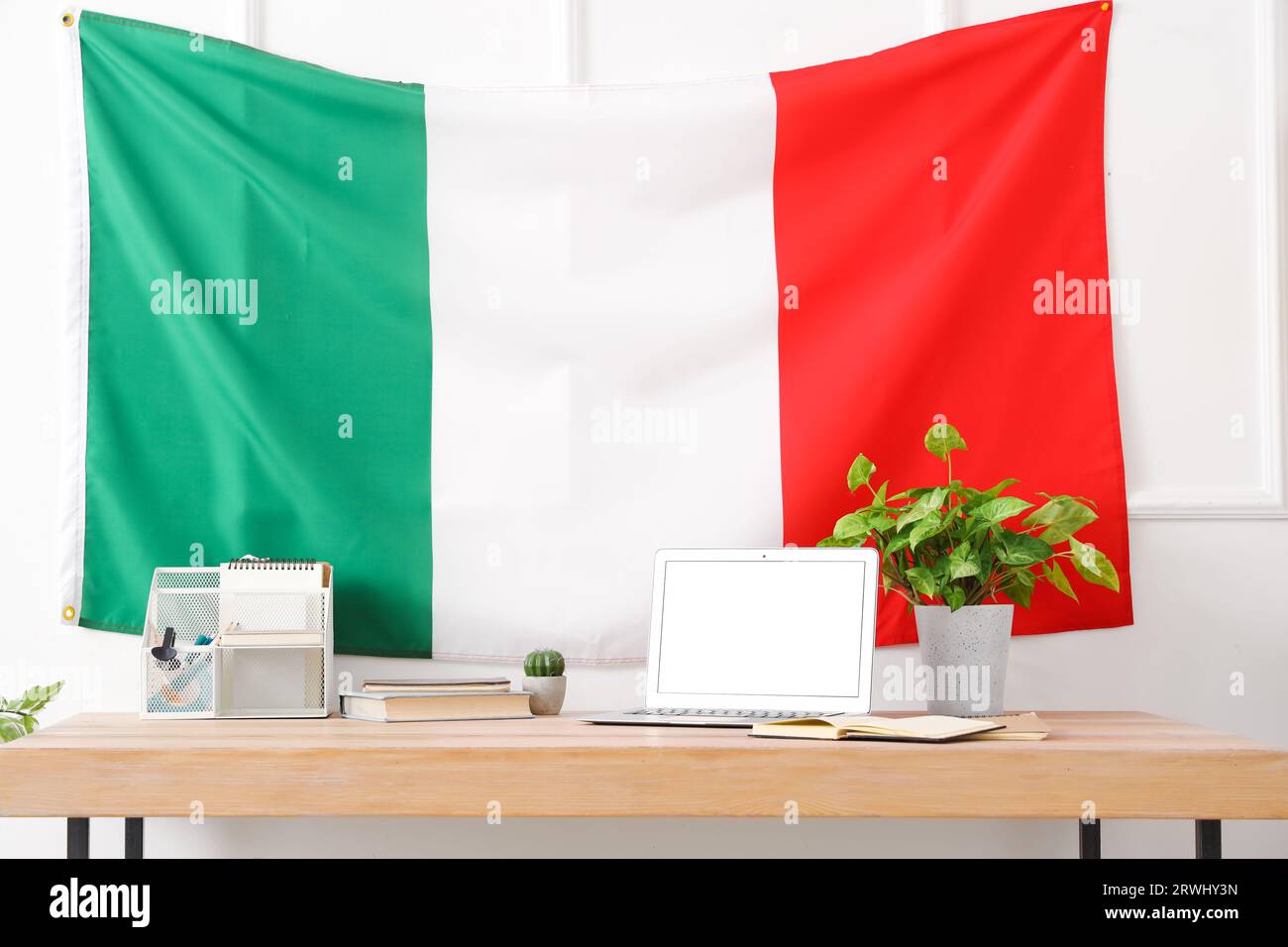Modern workplace with laptop, stationery and hanging Italian flag in ...
