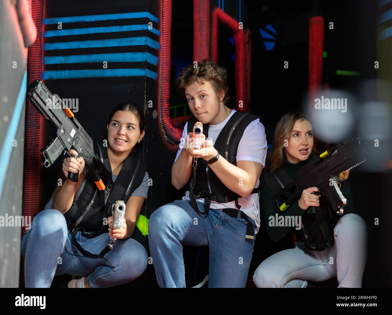 Modern young people with laser pistols playing laser tag on dark ...