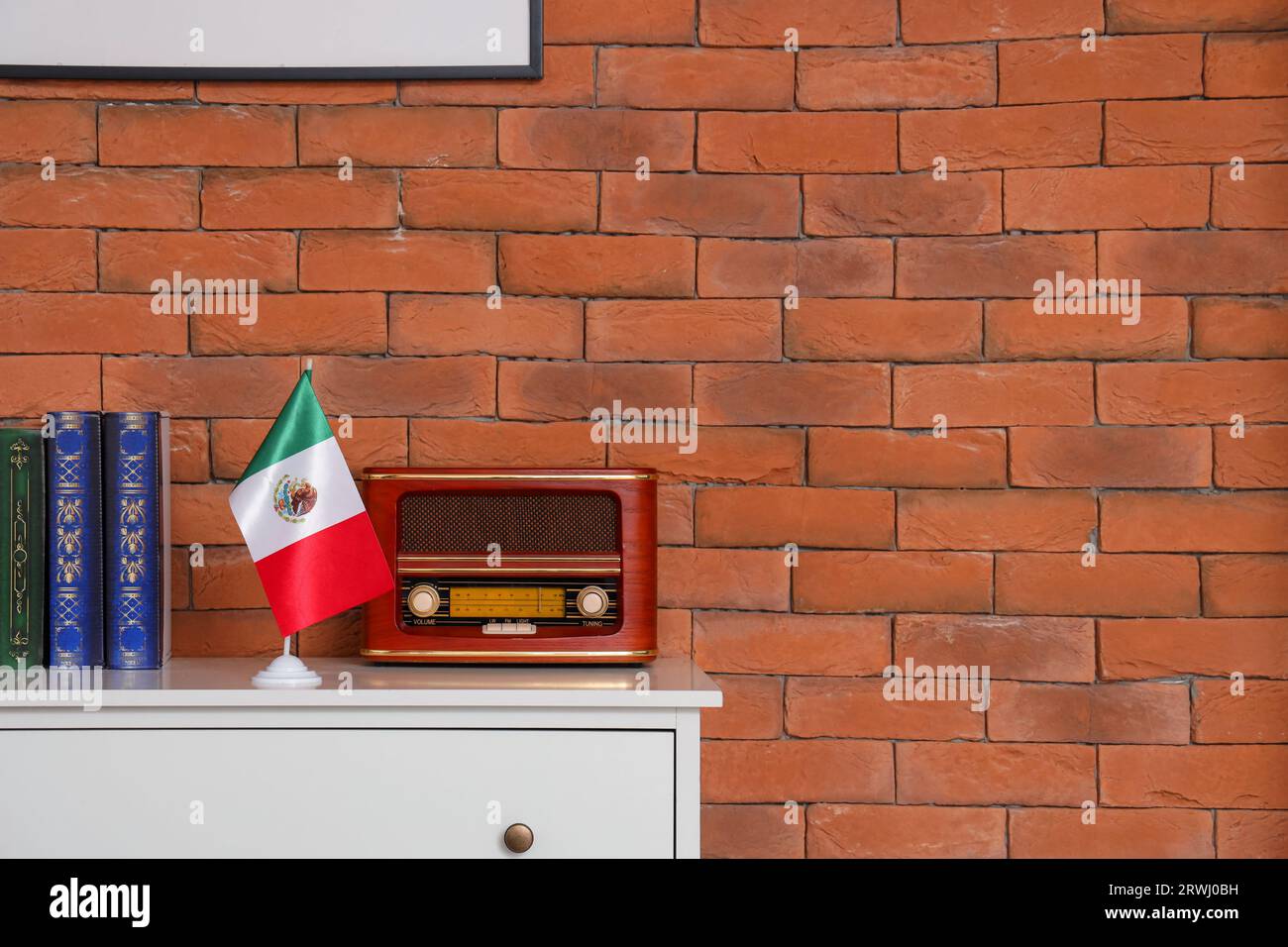 Retro radio receiver with Mexican flag and books on commode near brick ...