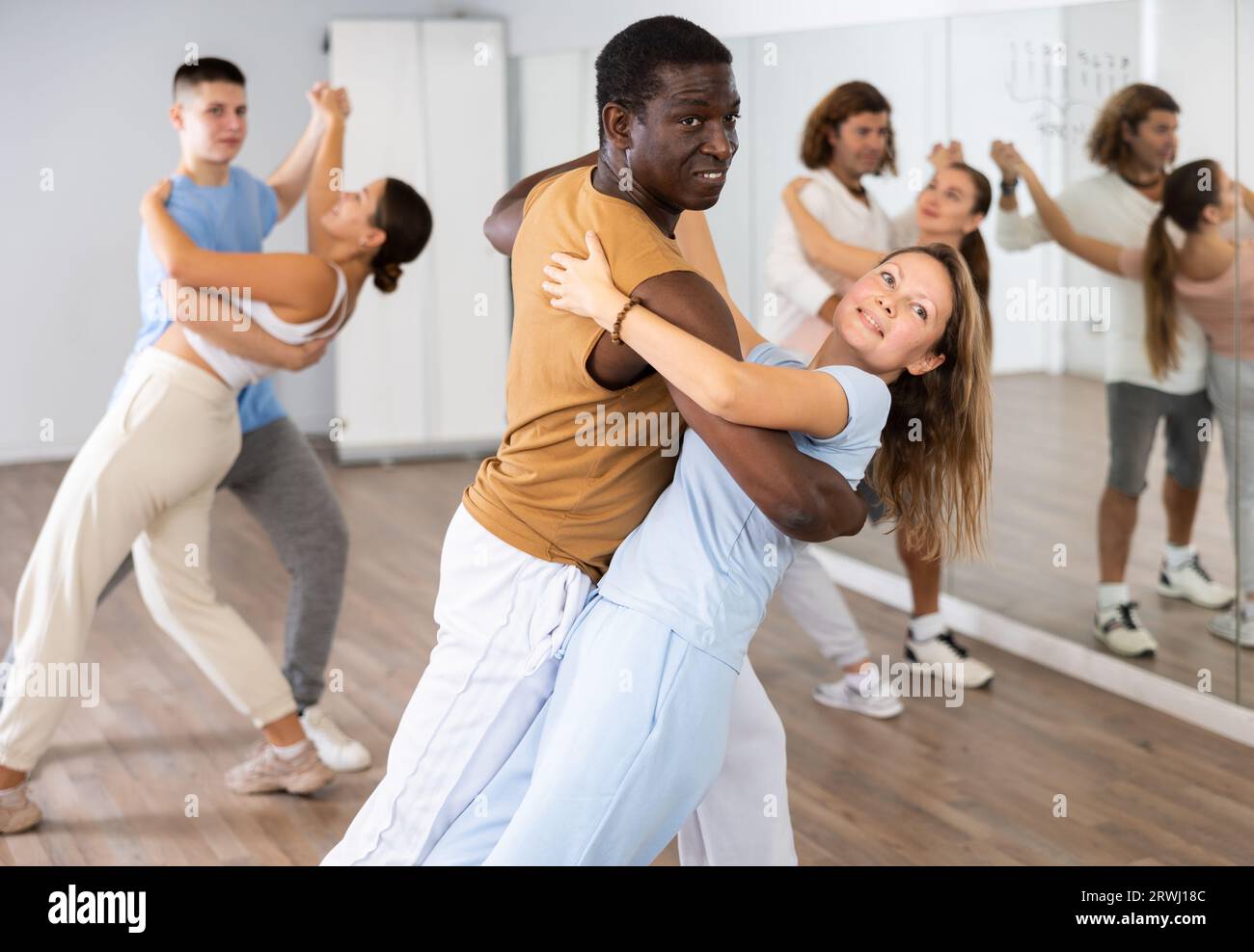 Positive middle-aged male partner leading young female in pair dancing ...