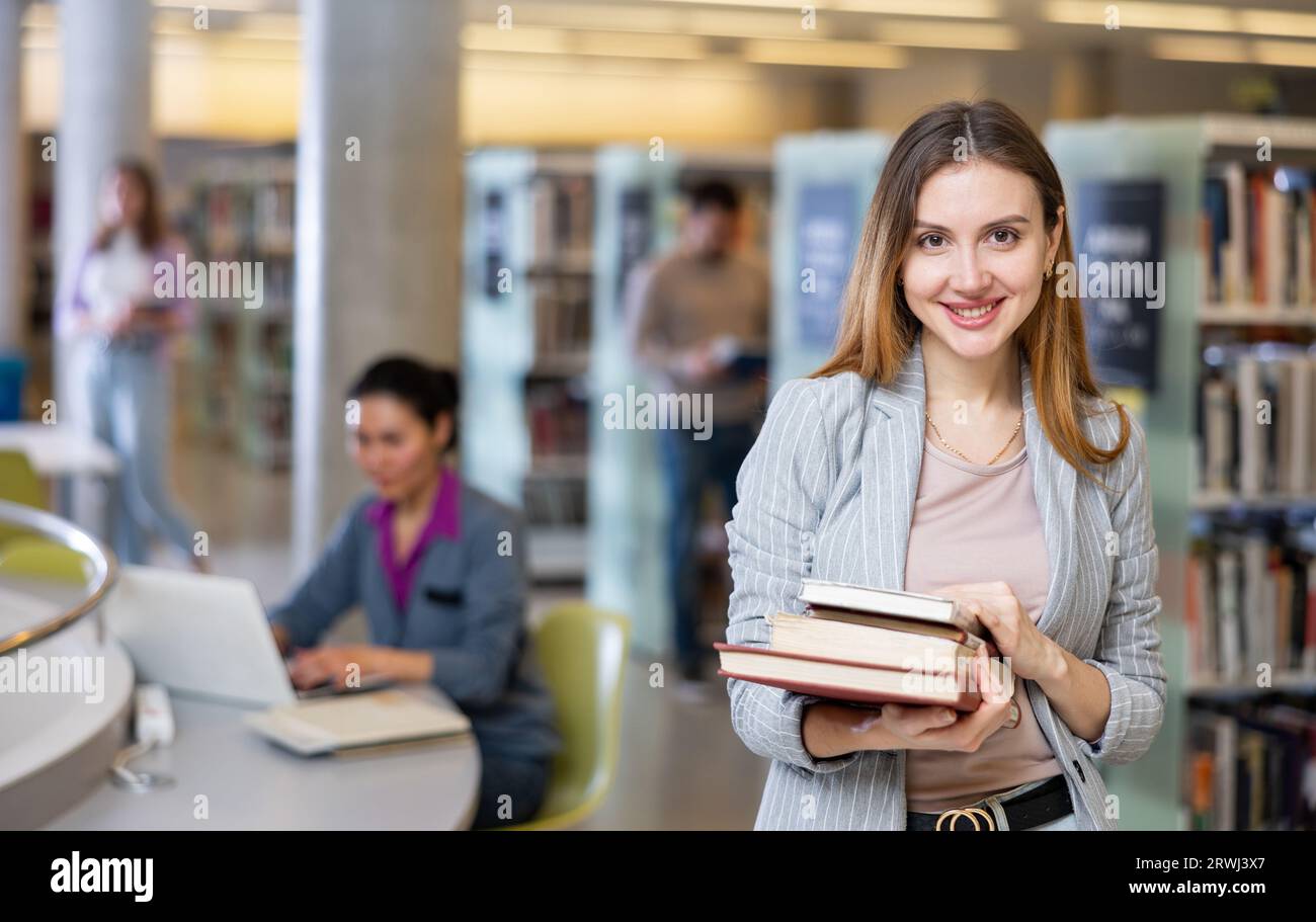 Successful female student standing with books in library Stock Photo ...