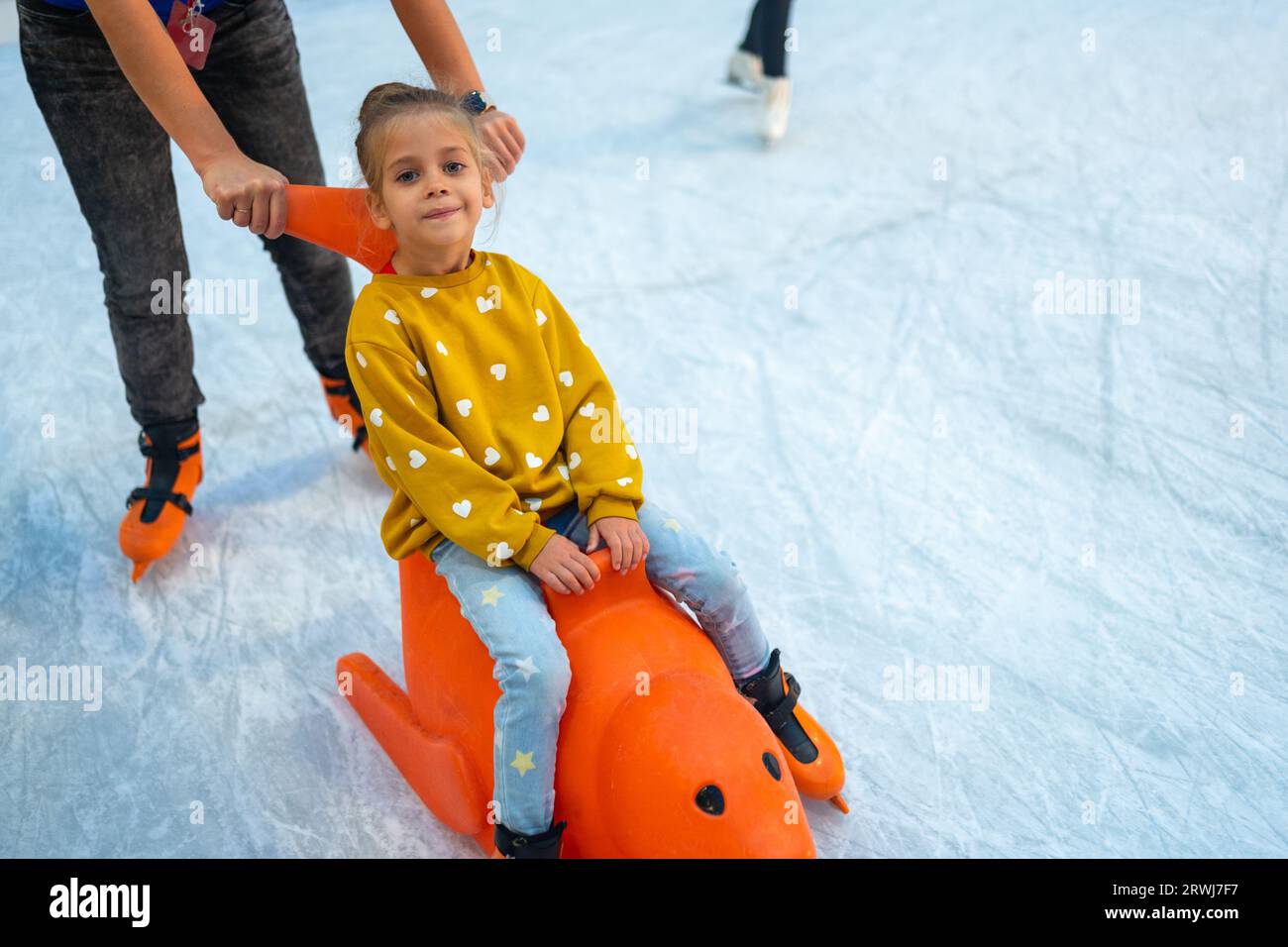 Kid using children plastic riding seal skate aid on skating ring. Child ...