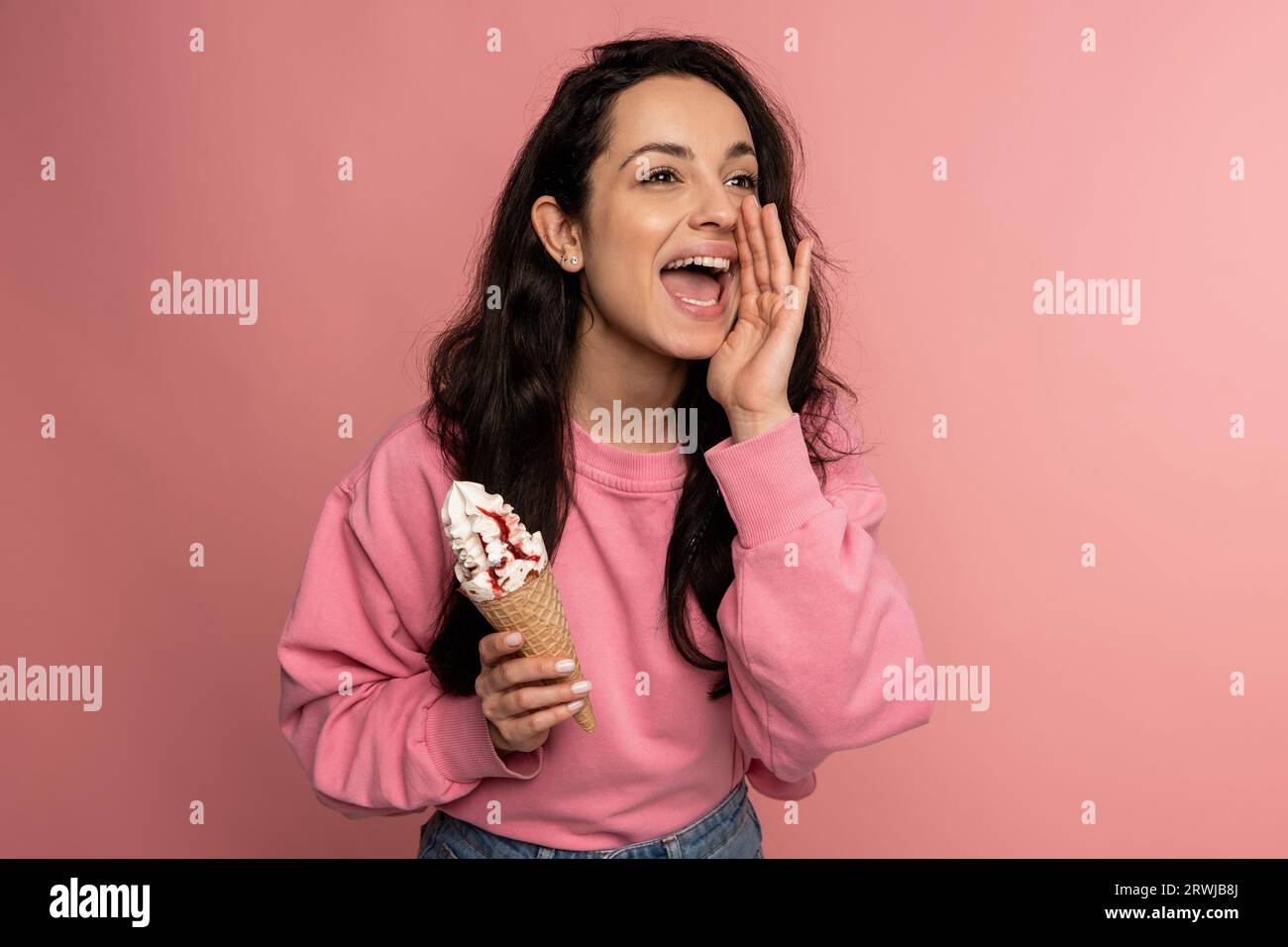 Young dark-haired female with the sundae in her hand hailing somebody ...