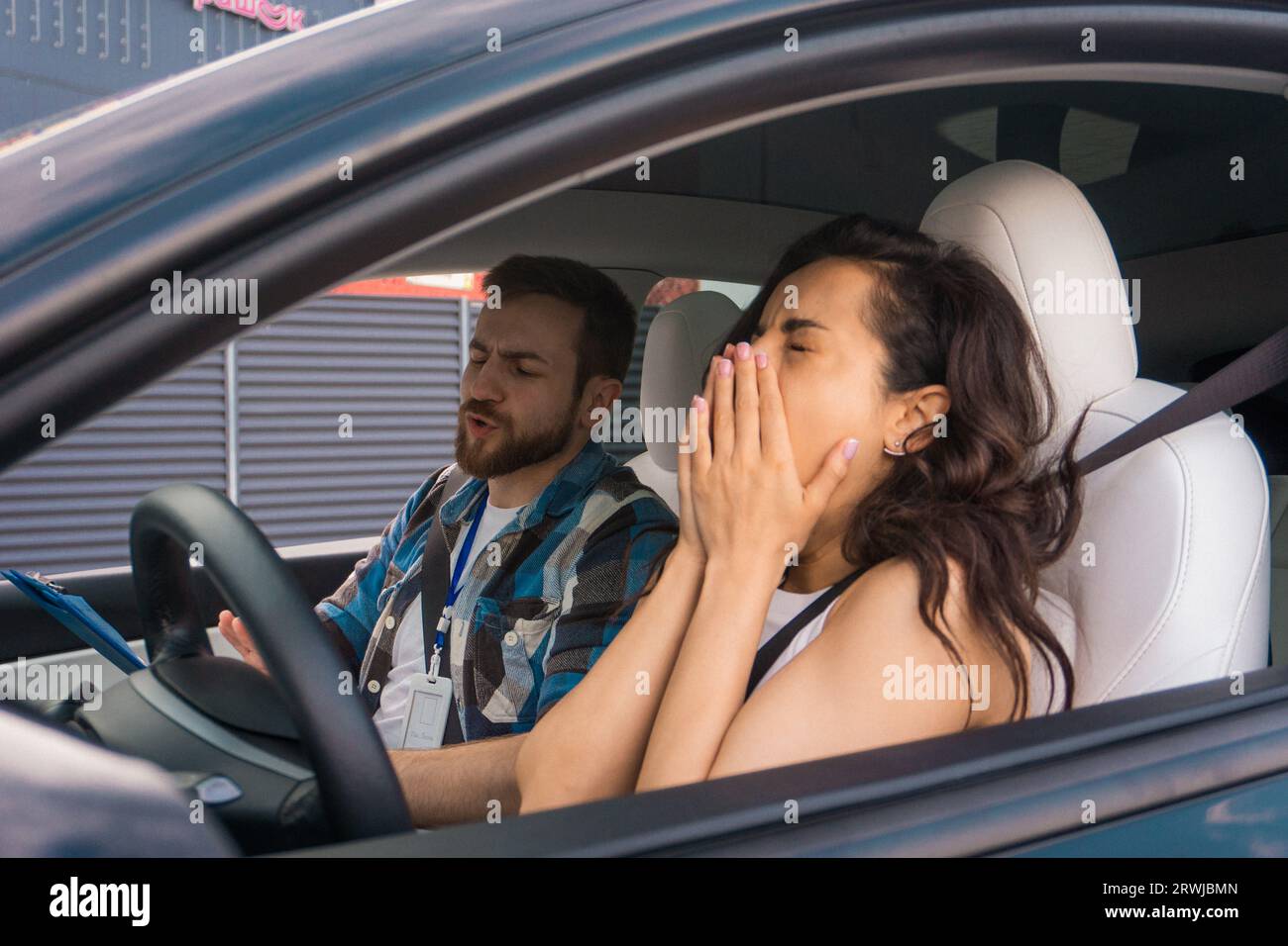 Male instructor teaching young woman to drive. Lady sitting in the car ...