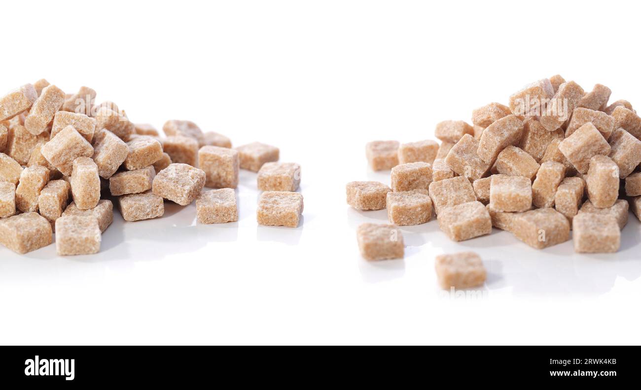 Two heaps of natural brown sugar cubes on white reflecting background ...