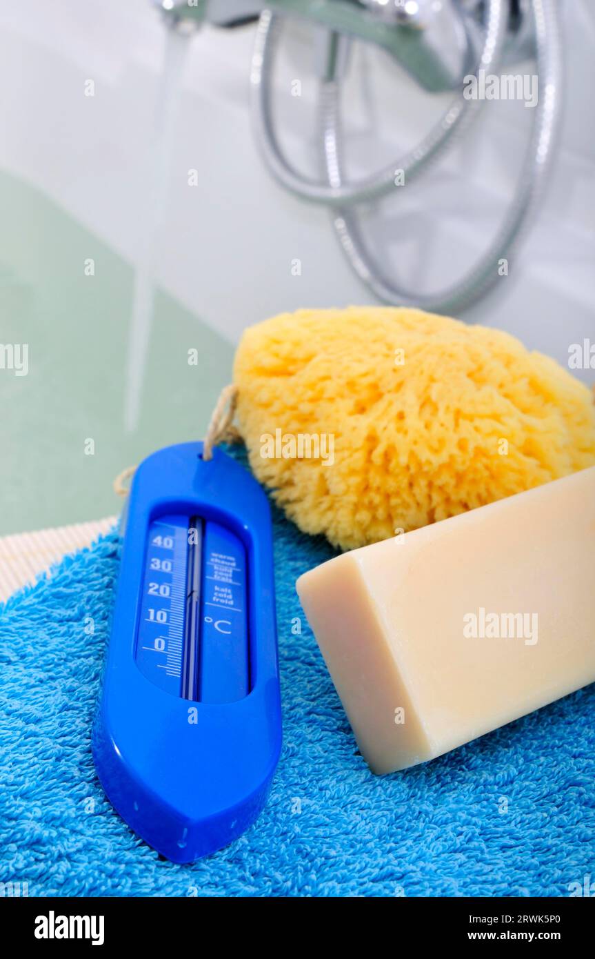 Towel, soap, sponge and thermometer in front of filled bathtub Stock ...