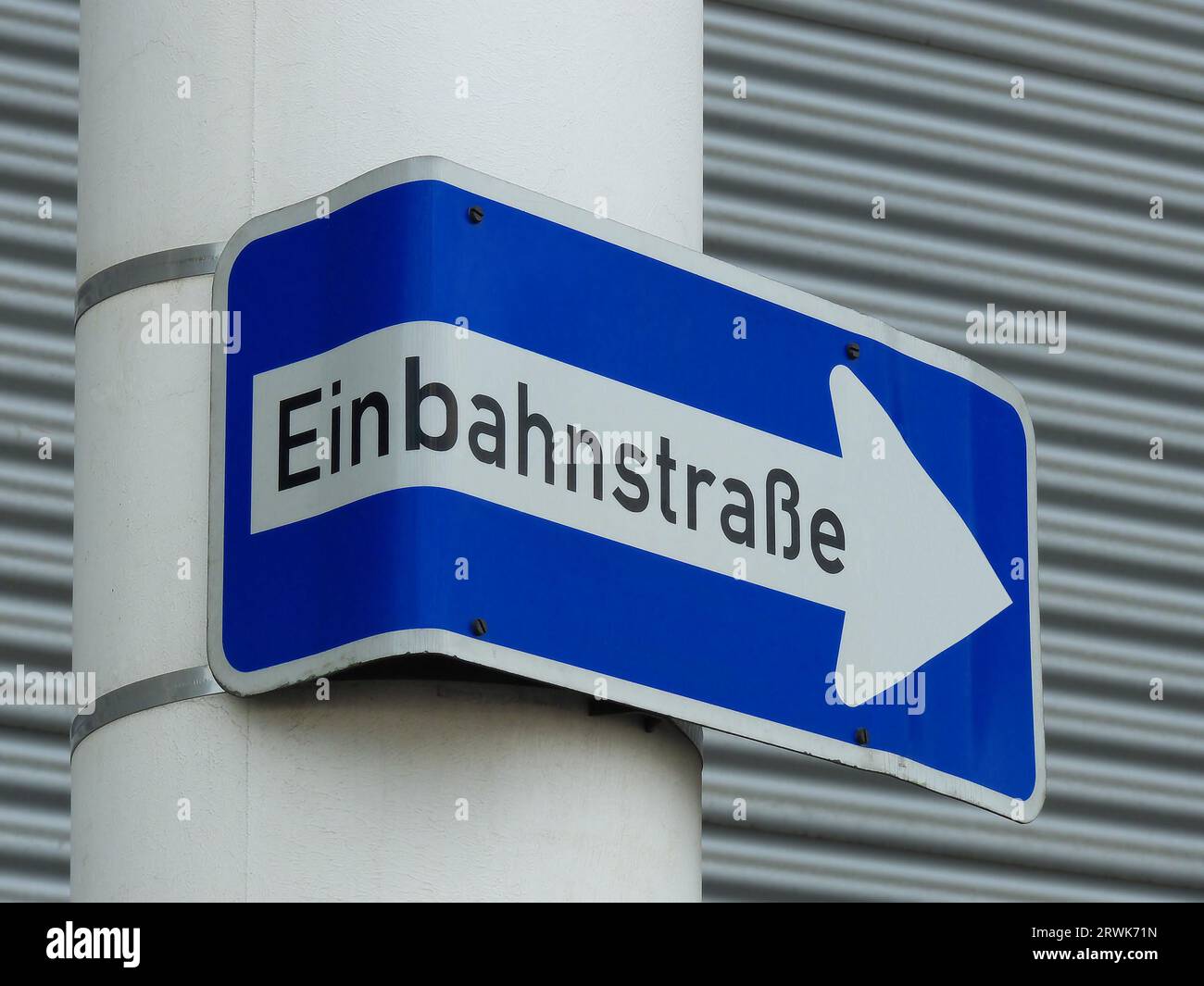 Bent one-way street sign on a white post, background grey slatted wall ...