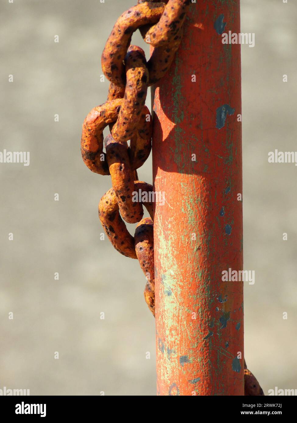 Somewhat rusty chain on a former orange iron post, background blurred ...