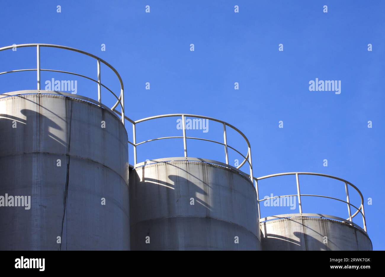 Three silos, sunlit, with shadows cast, detail, background bright blue ...