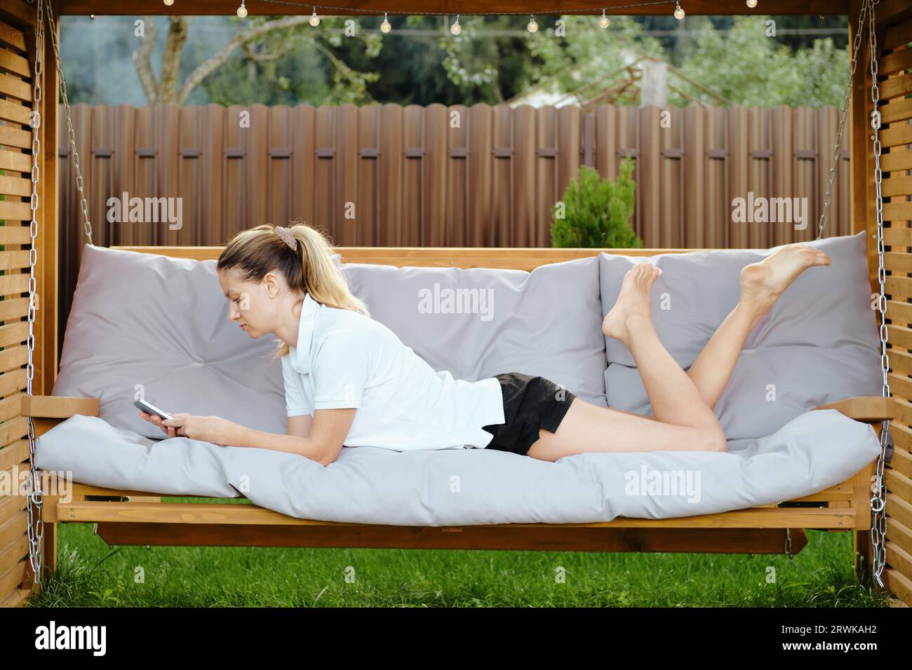 The woman is lying on her stomach on a cozy hanging bench, holding her ...