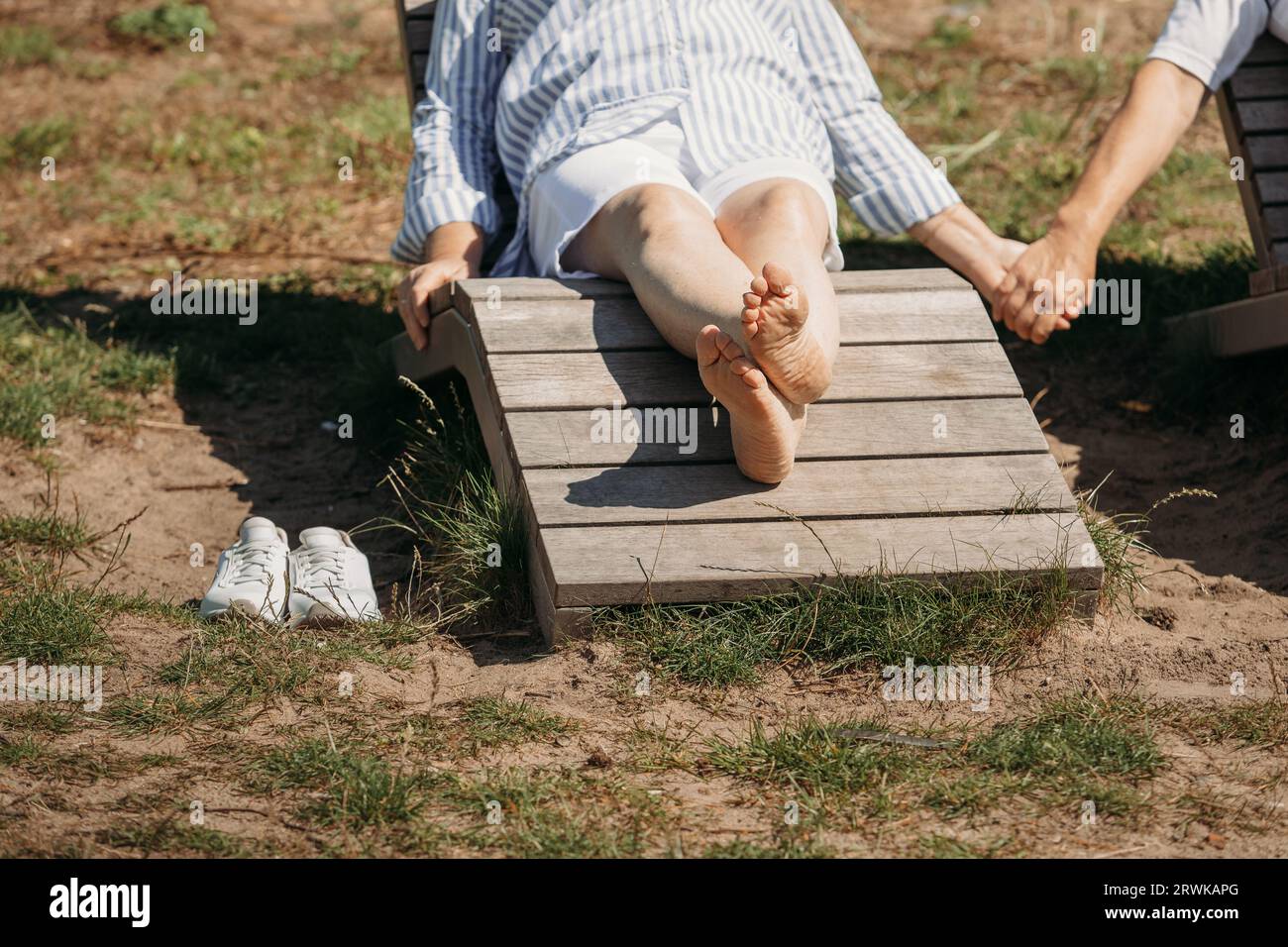 A couple of cute elderly people lie on sunbeds holding hands, basking ...