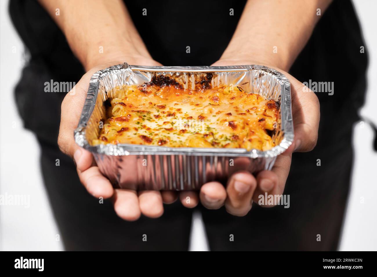 A human hand holding pasta macaroni schotel in an aluminum foil cup ...