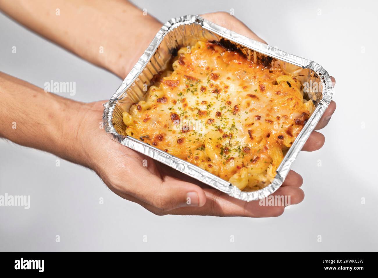 A human hand holding pasta macaroni schotel in an aluminum foil cup ...