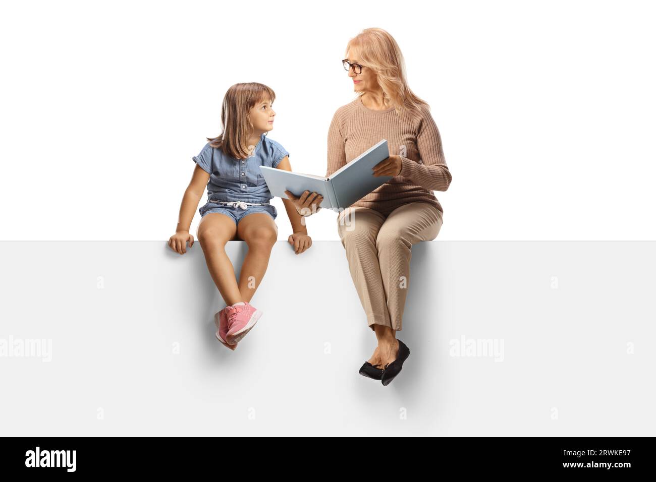 Woman reading a book to a little girl and sitting on a blank panel ...