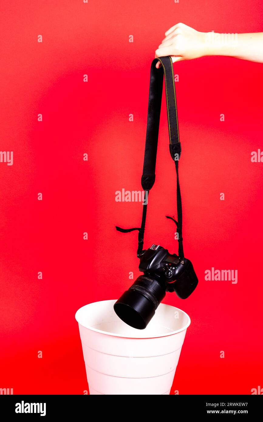 Hand with old digital camera in a trash can, isolated on a red ...