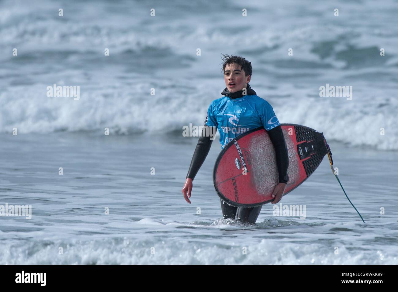 A young male surfer carrying his surfboard and walking out of the sea ...