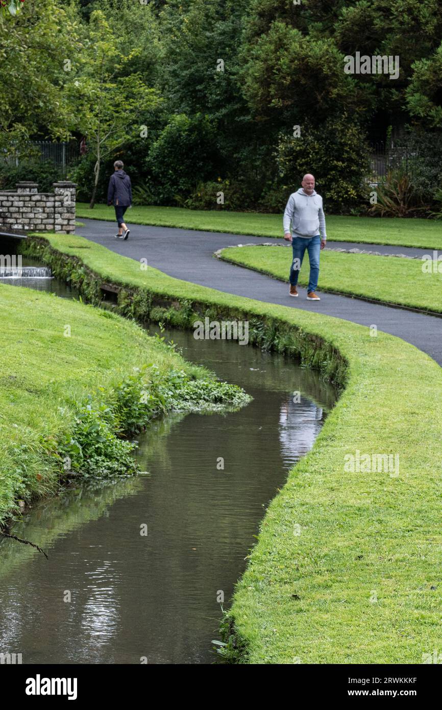 People walking along a footpath next to a river stream flowing through ...