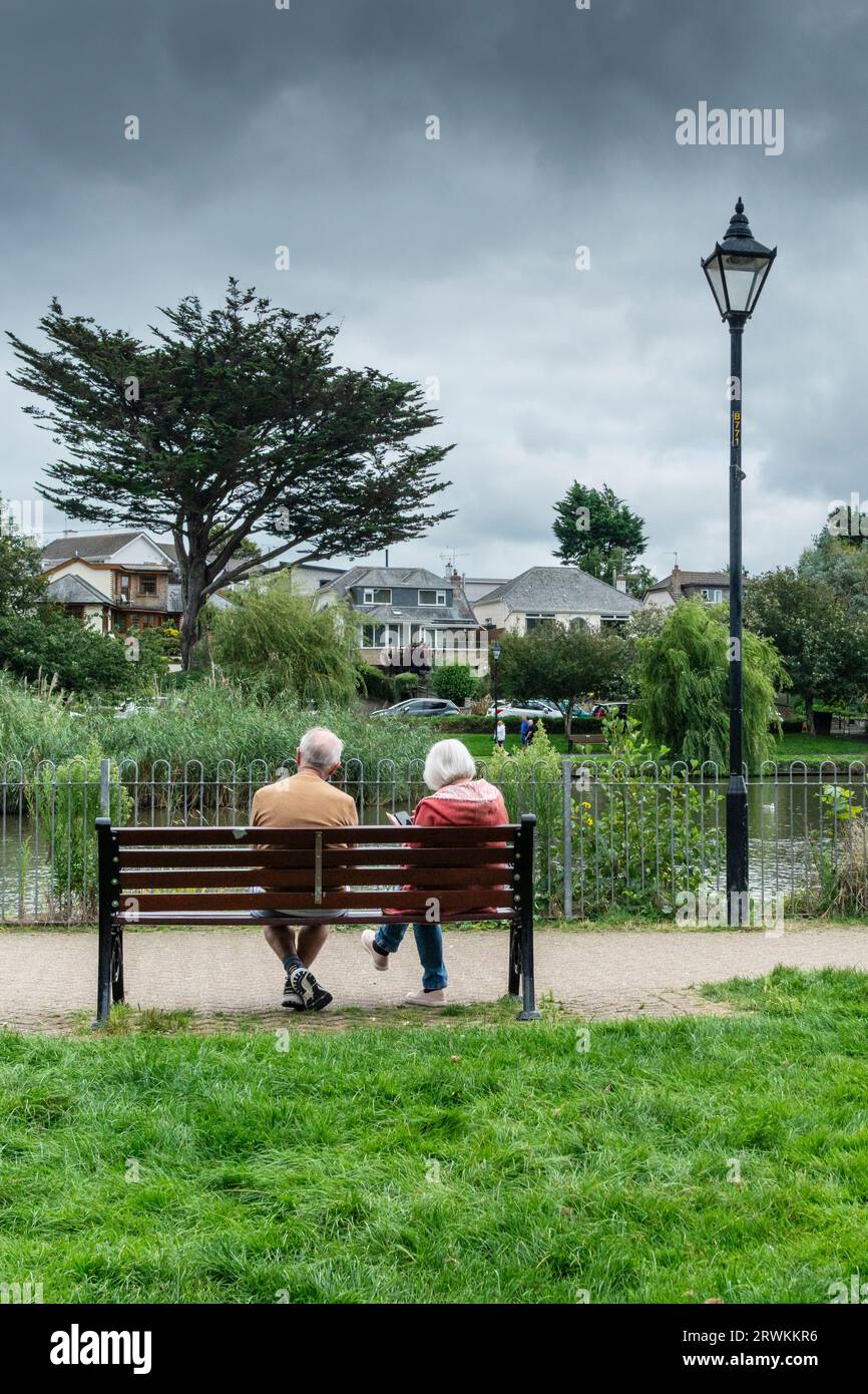 A couple relaxing on a bench overlooking Trenance Boating Lake in ...