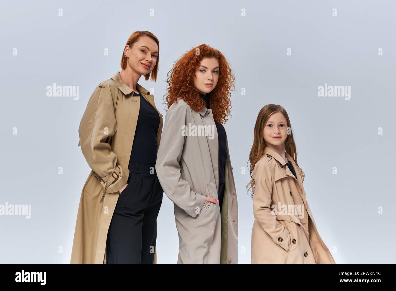 happy redhead family in coats posing with hands in pockets on grey ...