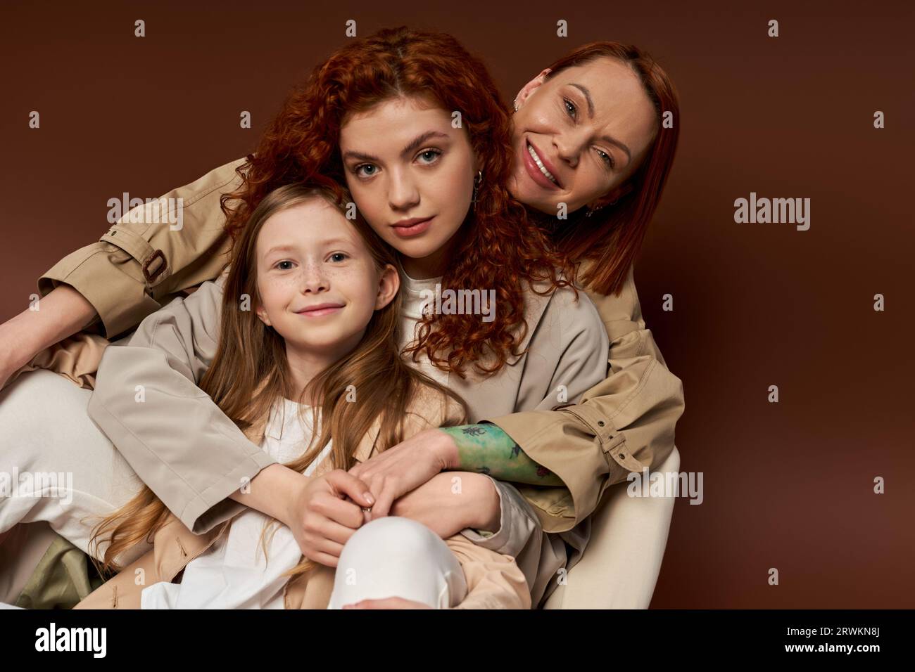 three generations, positive redhead family looking at camera on brown ...