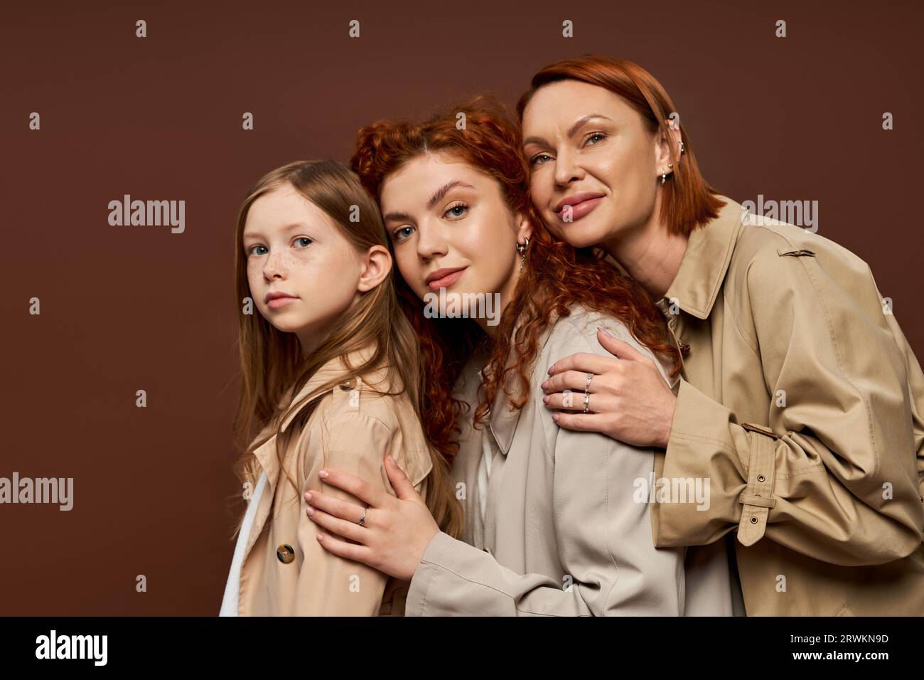 family of three female generations with red hair posing in beige coats ...