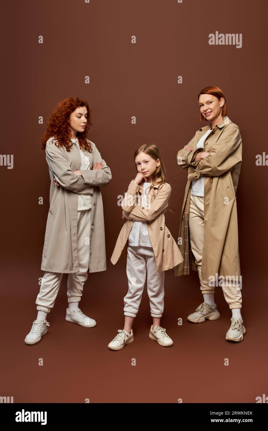 three generations, women in coats posing and looking at girl on brown ...