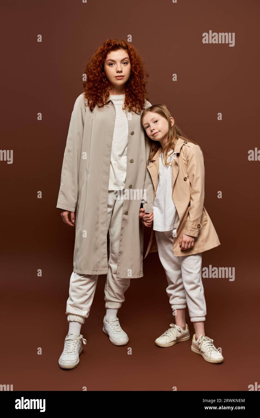 two generations, curly mother holding hands with daughter and standing ...