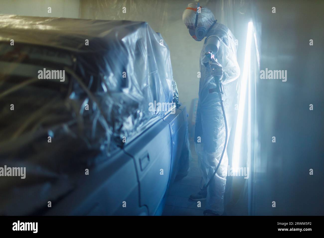 Car painter in protective clothes and respirator mask painting vehicle ...