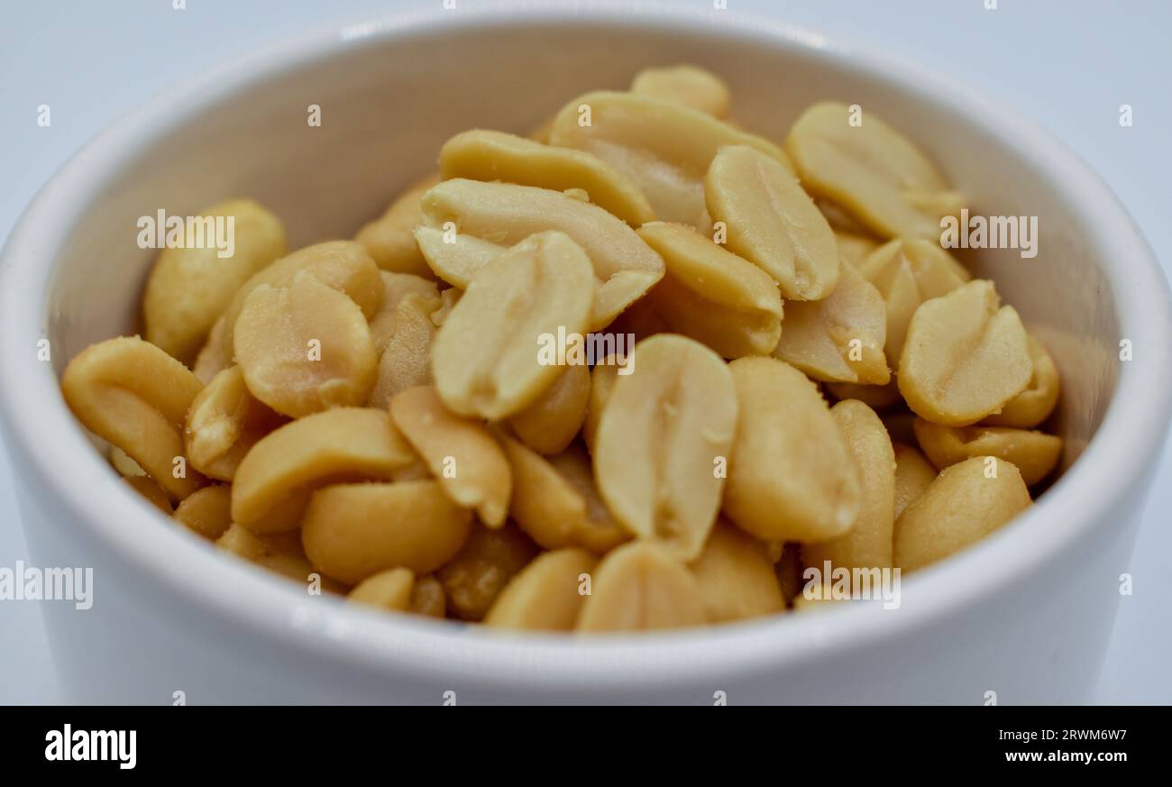 Some peanuts that have been poured into a small white bowl for a snack ...
