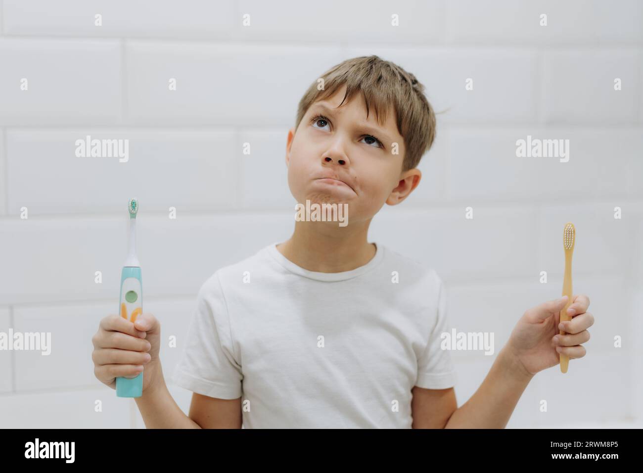 cute 8 years old boy holding bamboo and electric tooth brush making ...