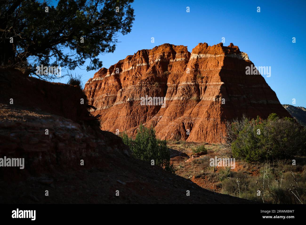 A dramatic landscape featuring a large hill of red rocks rising out of ...