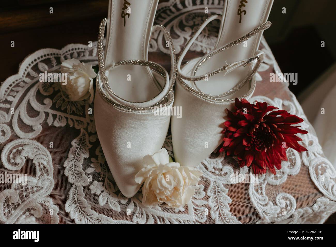 A pair of white bridal shoes placed atop a lace tablecloth featuring a ...