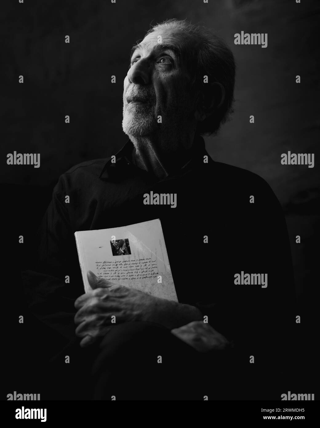 A senior man looking up while holding a book in grayscale in Tehran ...
