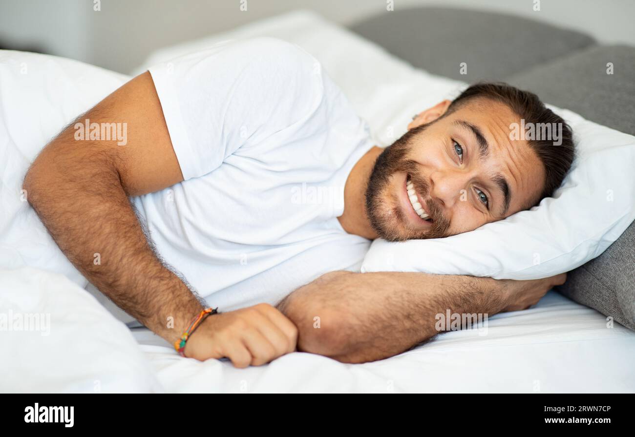 Portrait of happy handsome millennial man lying on bed Stock Photo - Alamy