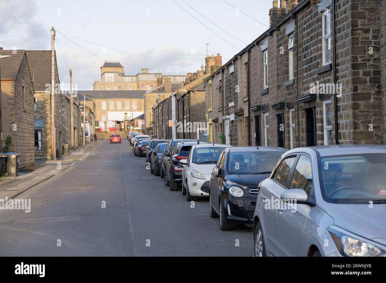 a red car drives pass a row of parked cars outside stone terrace house ...