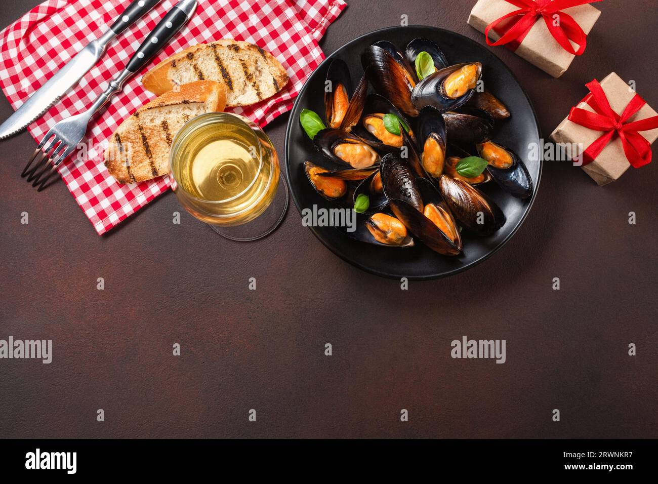 Seafood mussels and basil leaves in a black plate with wineglass, fork ...