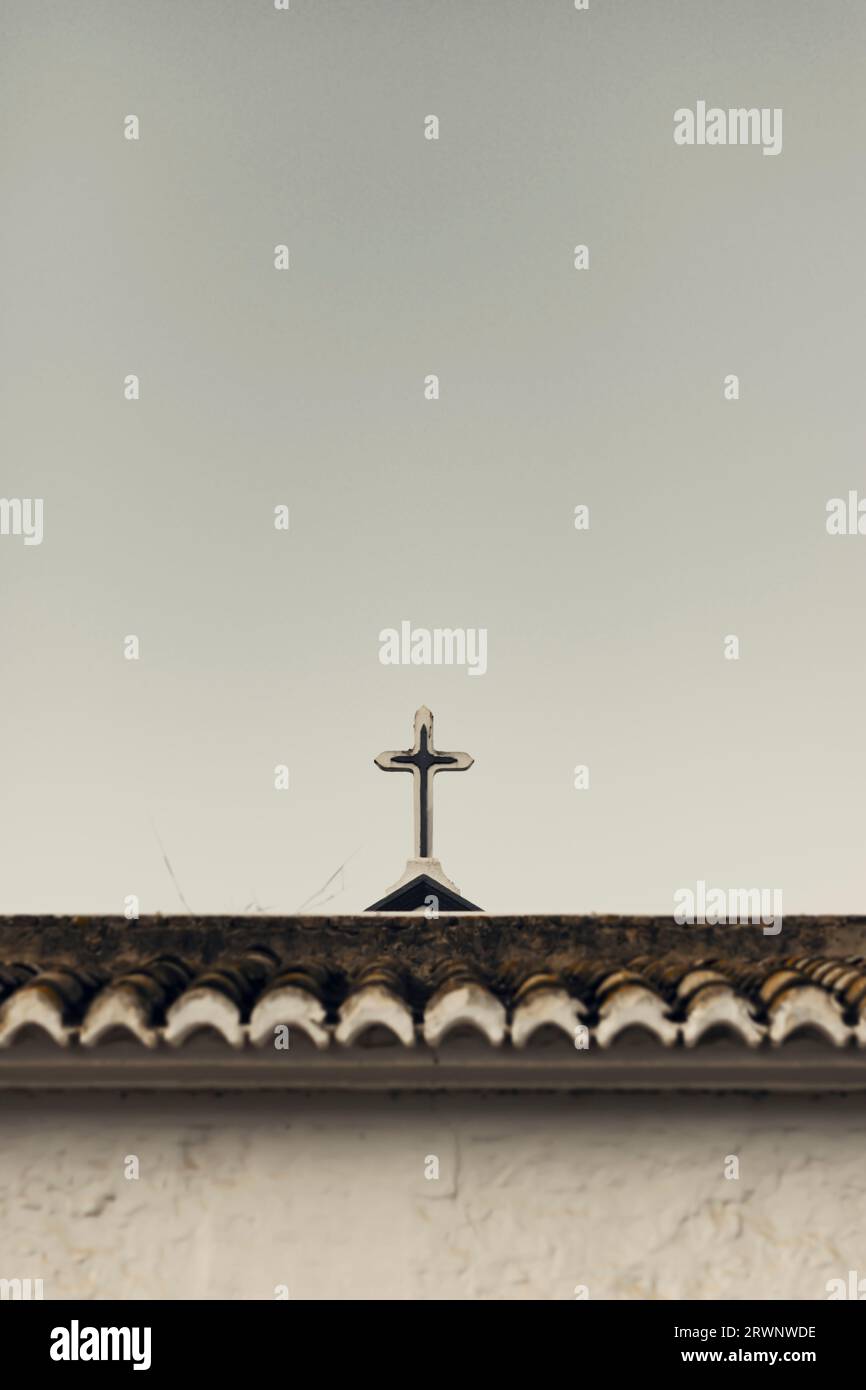 Lone Christian cross seen above the roof of a cemetery wall, with dark ...
