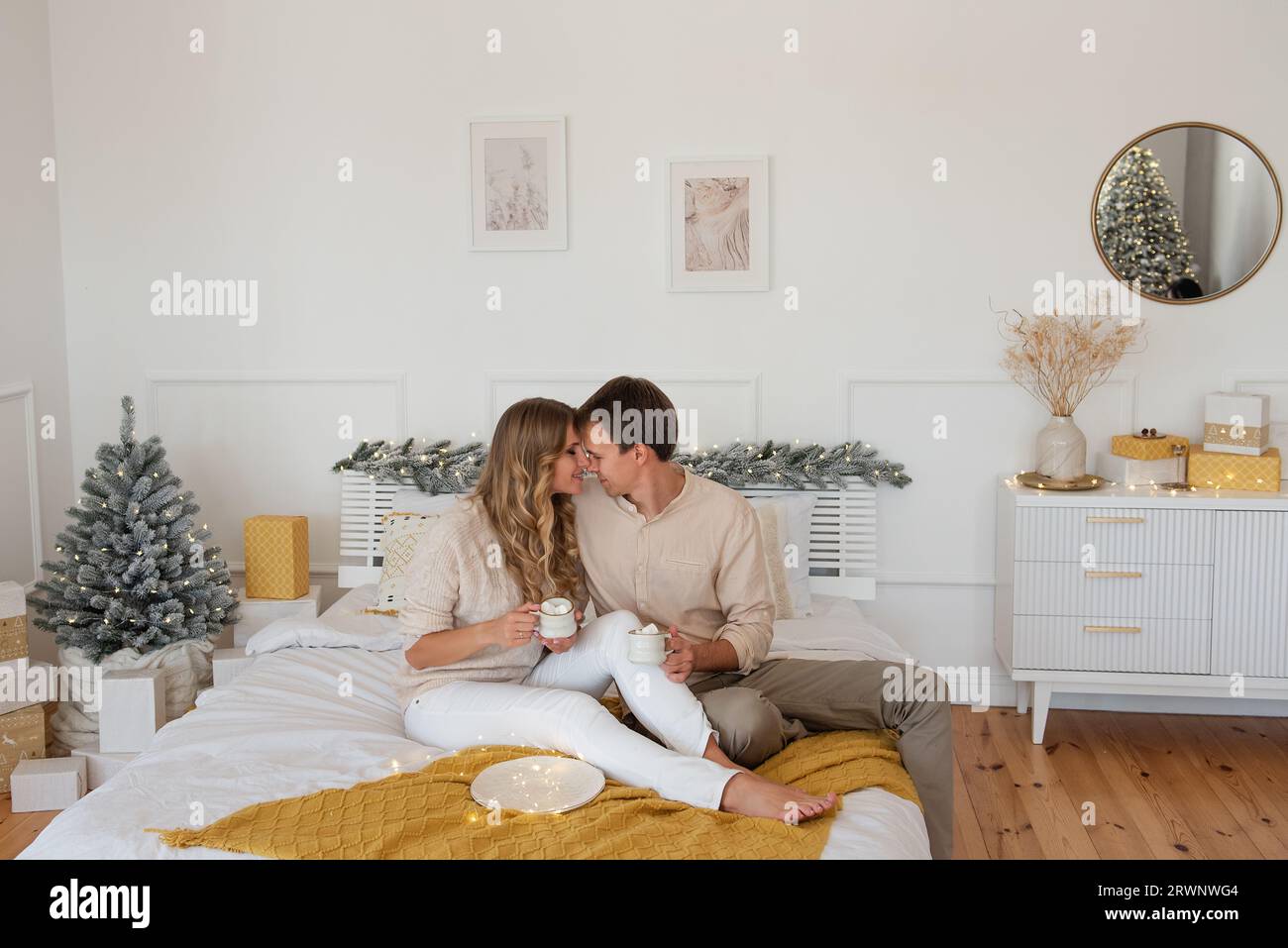 Cute, cheerful couple cuddling on bed with yellow blanket on Christmas ...