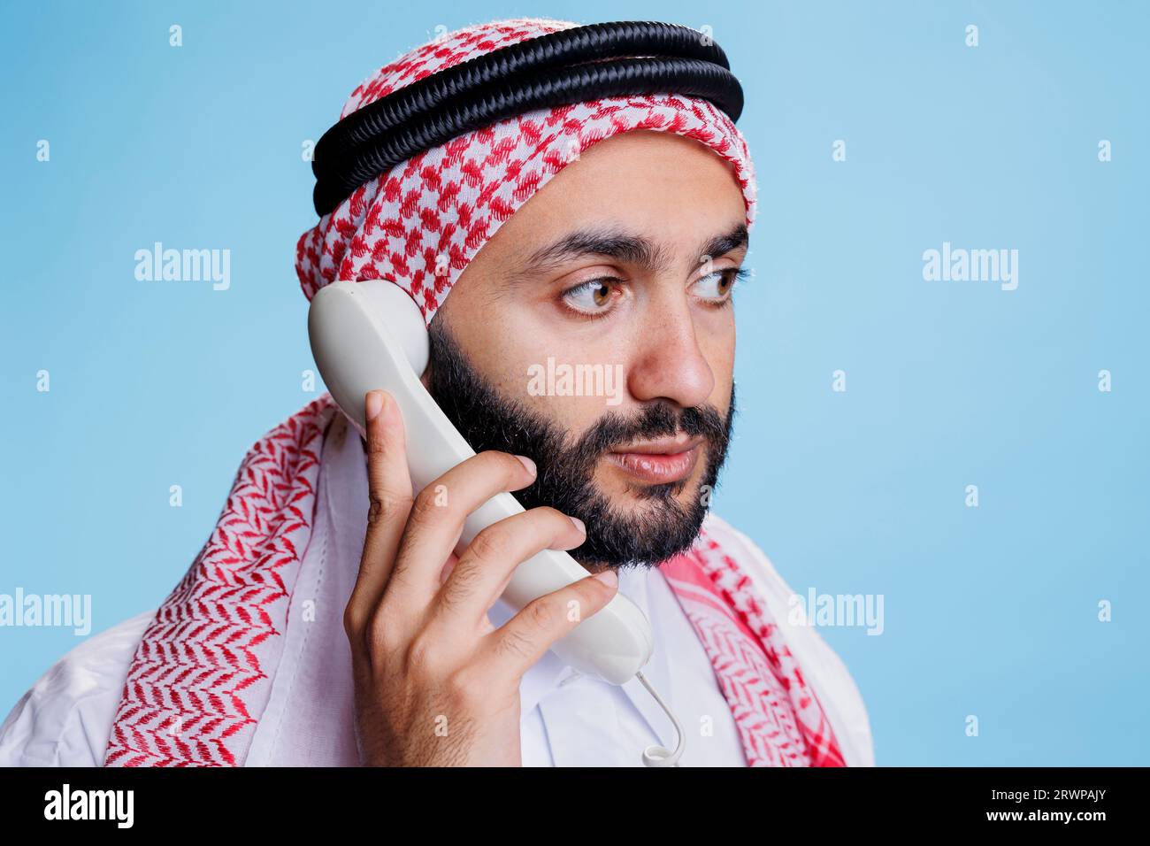 Muslim man wearing traditional checkered scarf speaking on landline ...