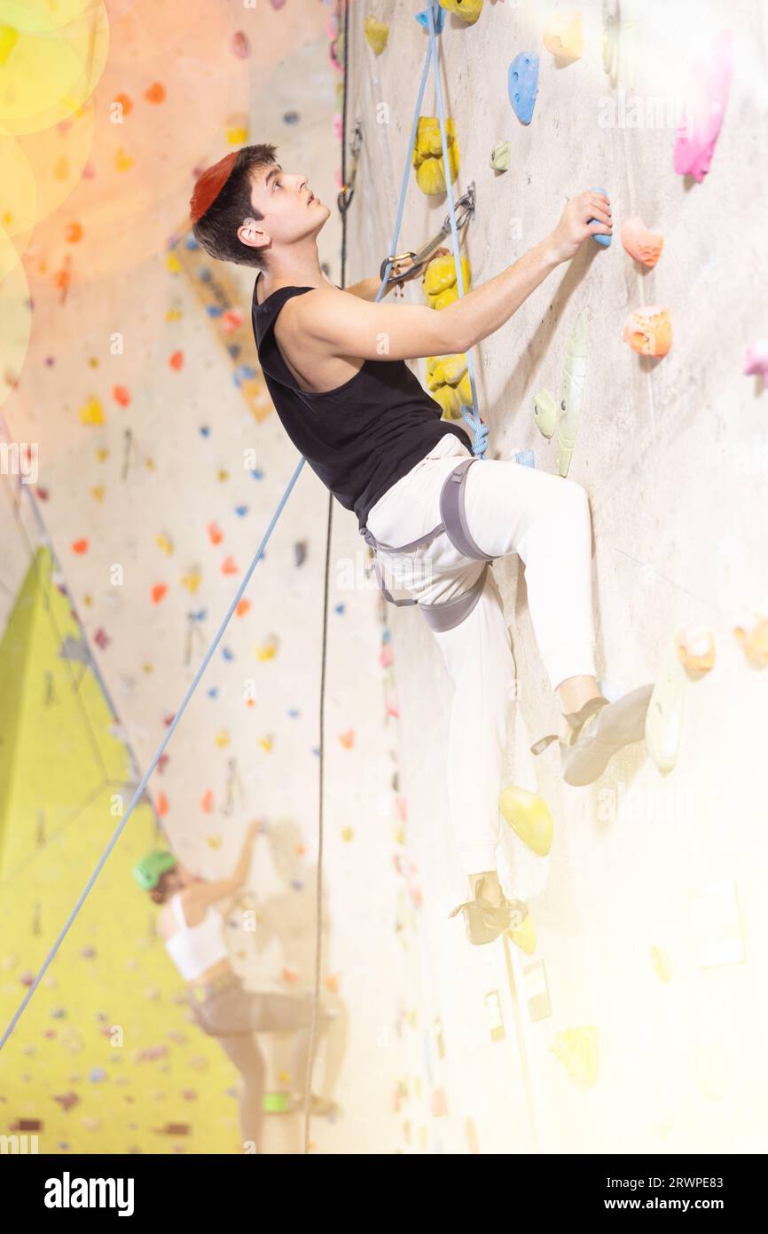 Positive extreme young guy with rope training on concrete climbing rock ...