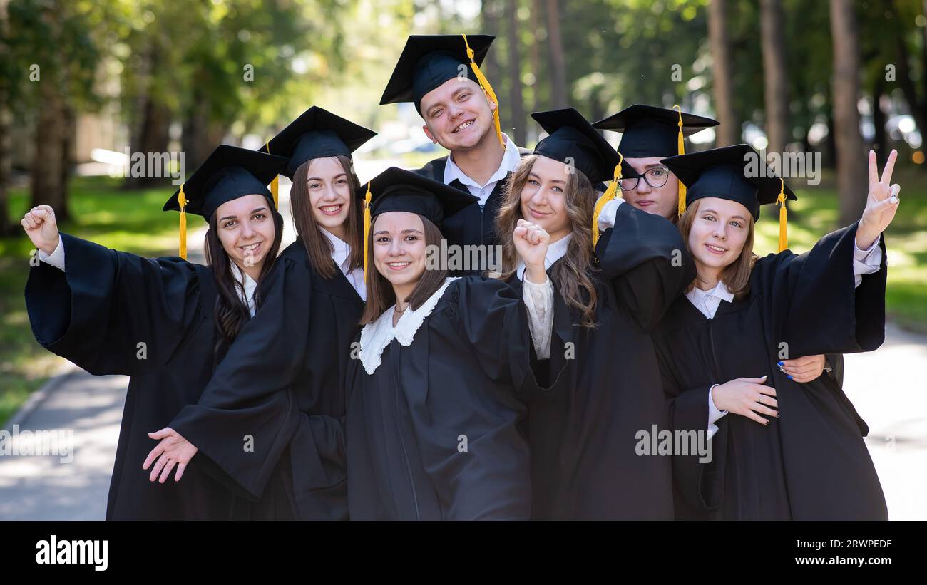 Group of happy young people in graduation gowns outdoors. Students are ...