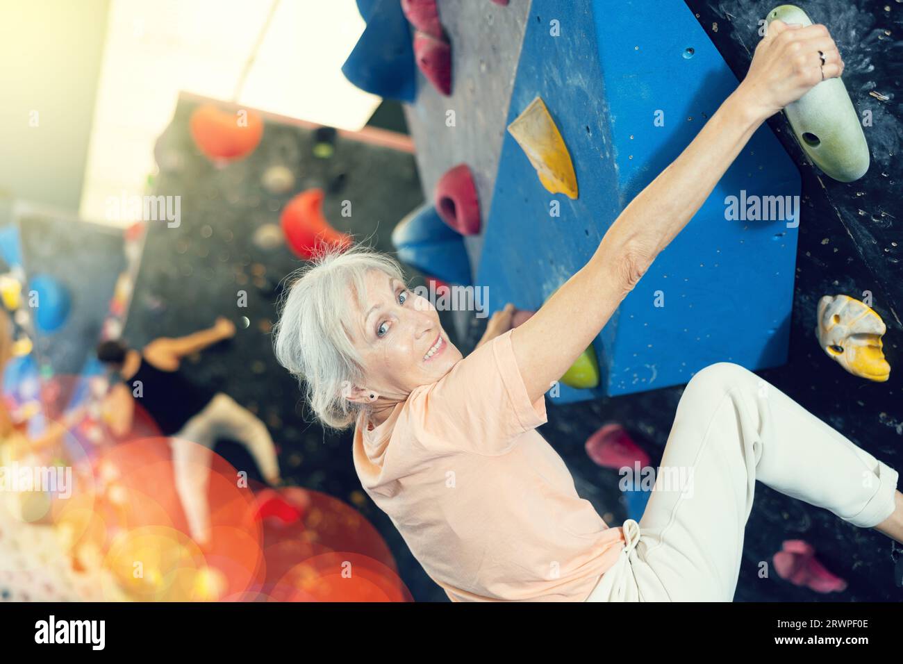 Mature female fitness climber training at bouldering gym.Woman rise up ...