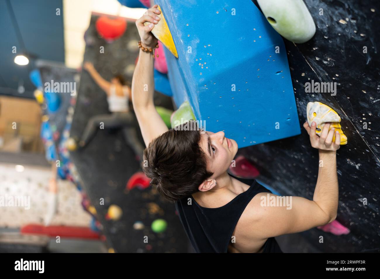 young muscular male sportsman climbing black wall for bouldering in gym ...