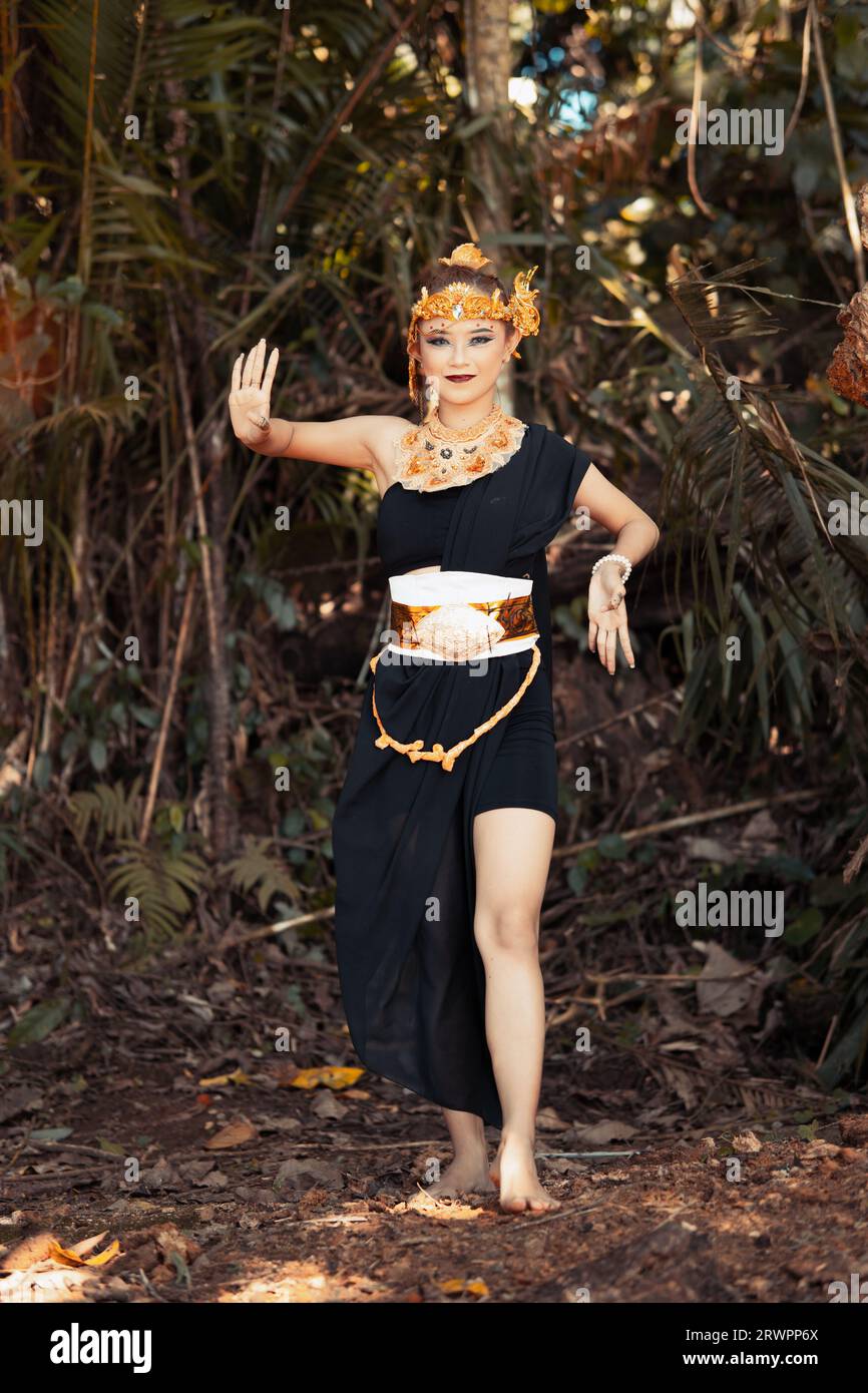 Javanese woman dancing pose in a black tank top and black skirt with golden crown and golden ...