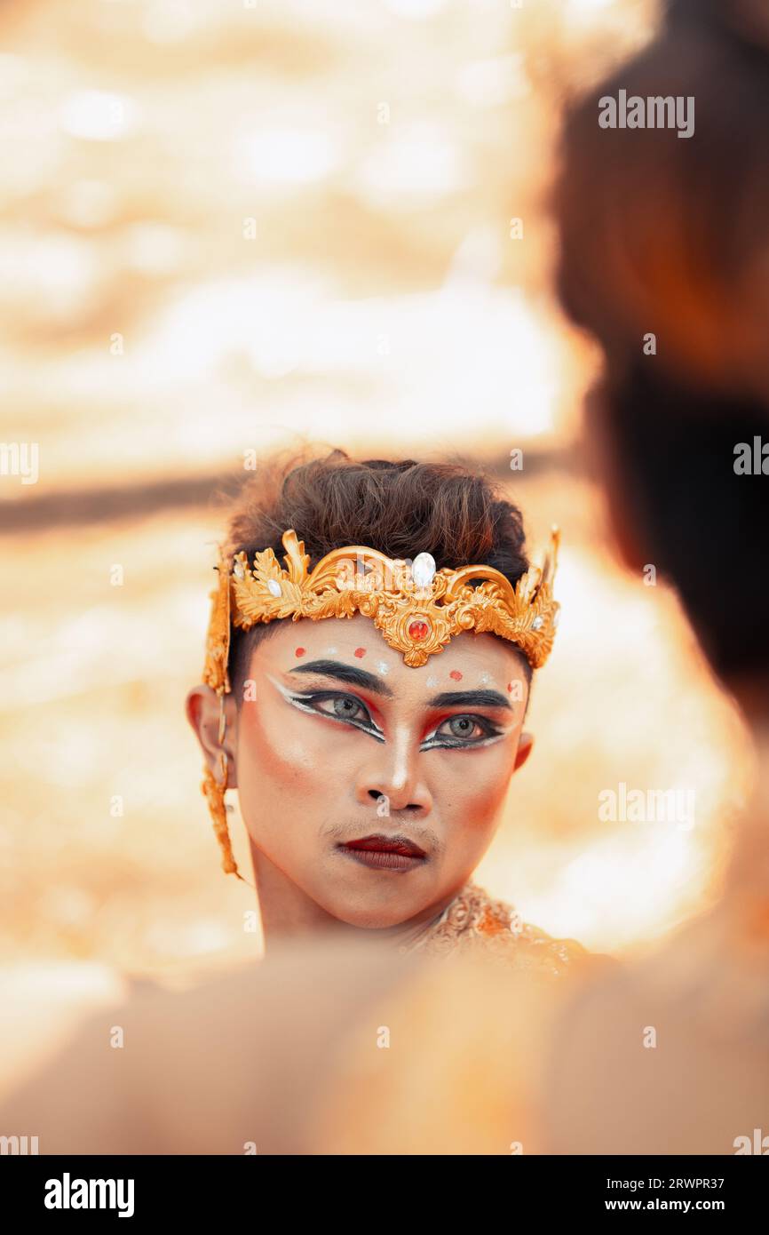 An Asian man faces in makeup with a golden crown on her head looks ...