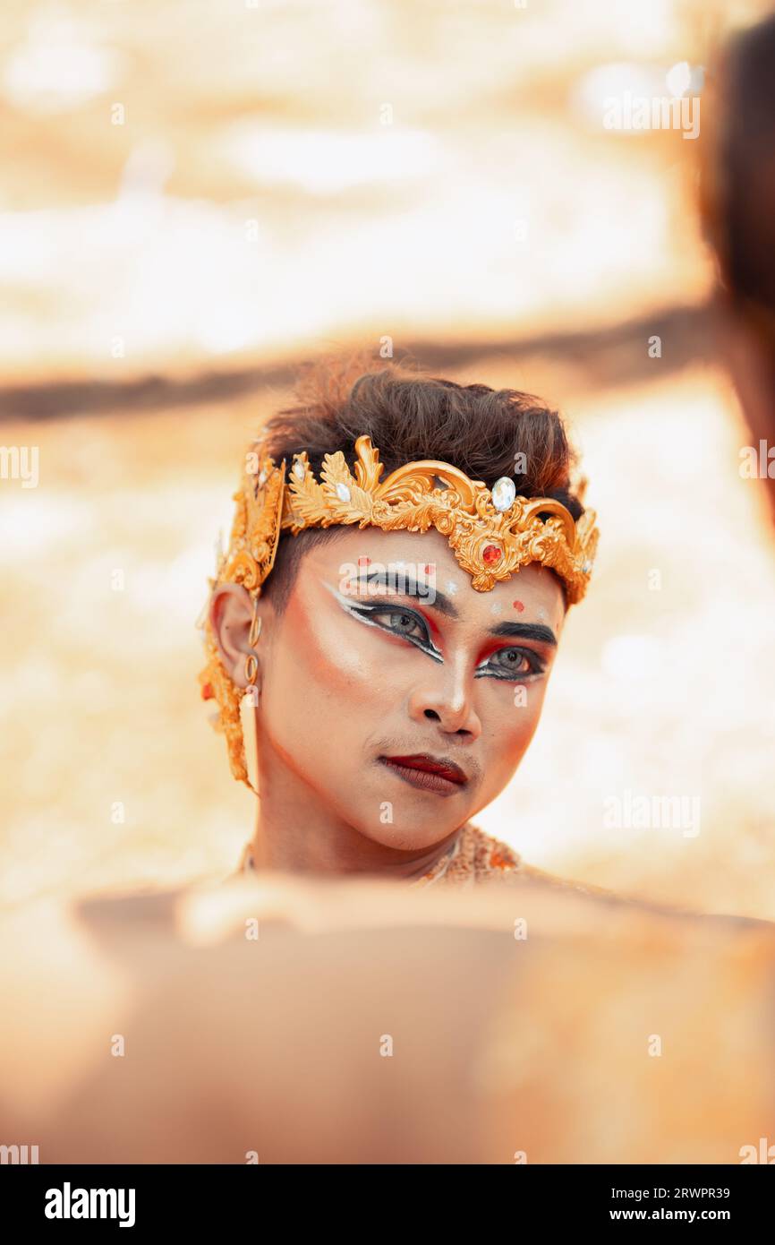 An Asian man faces in makeup with a golden crown on her head looks ...