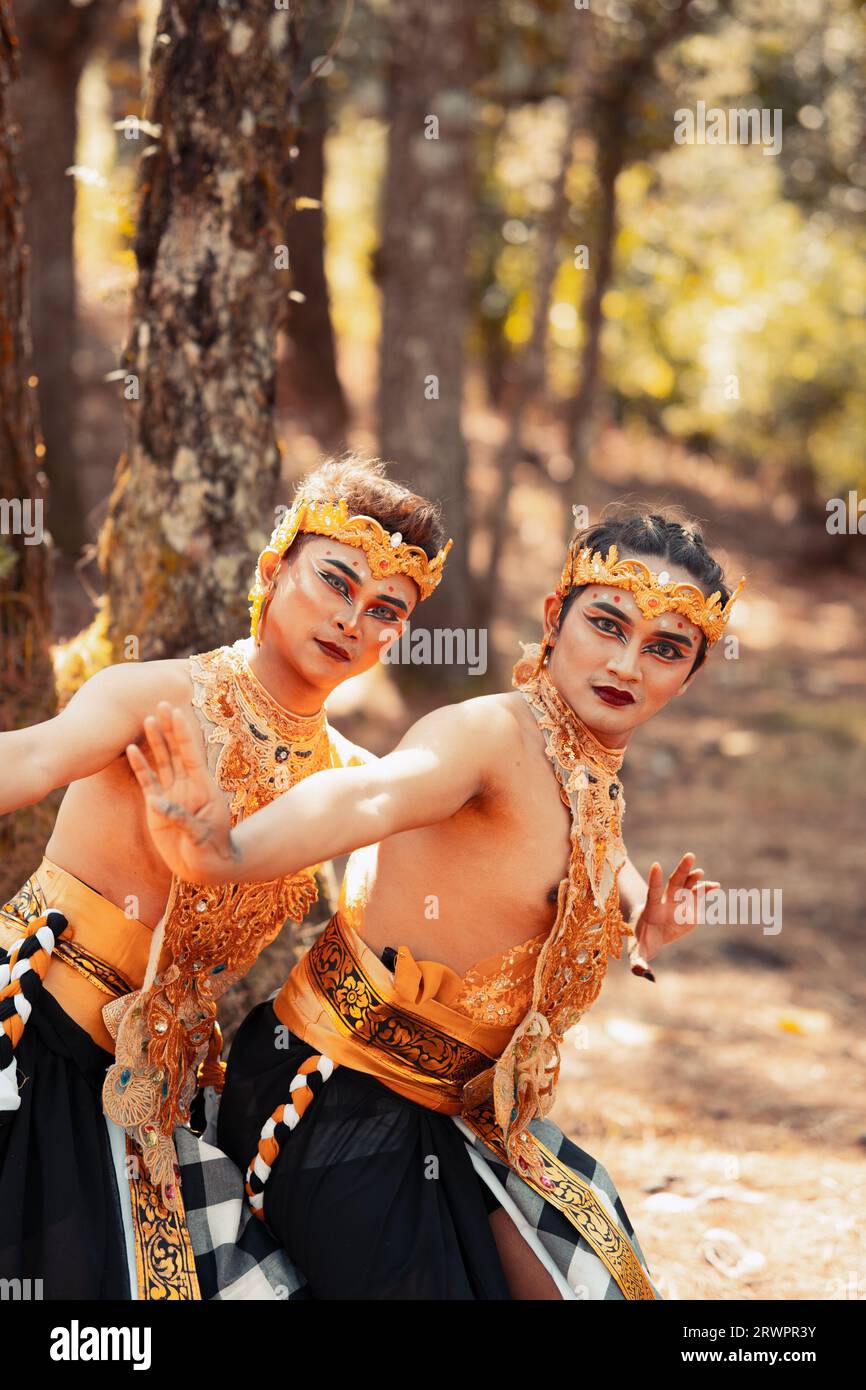 Two Balinese men dancing together in front of the tree while wearing a ...