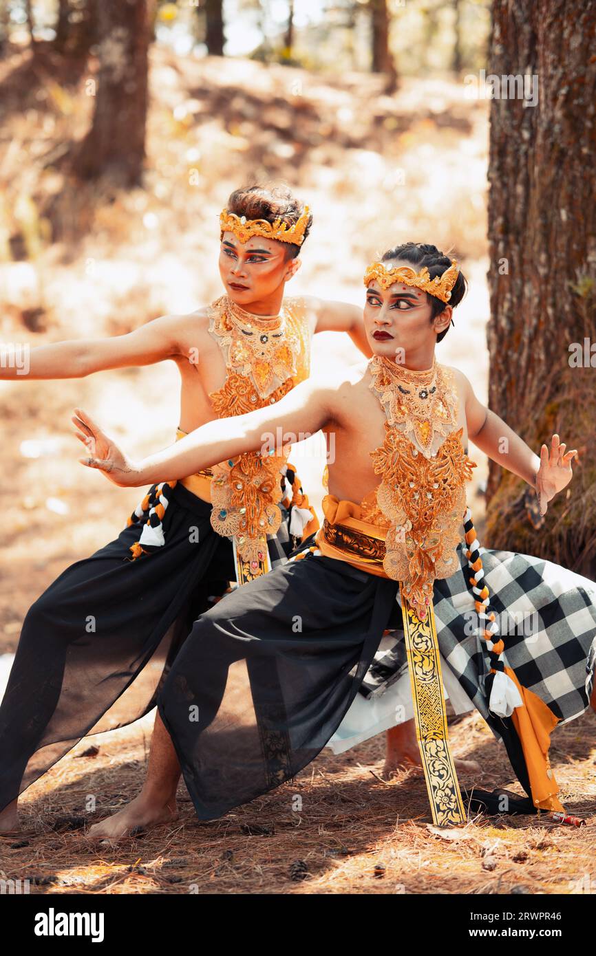 Two Balinese men dancing together in front of the tree while wearing a ...