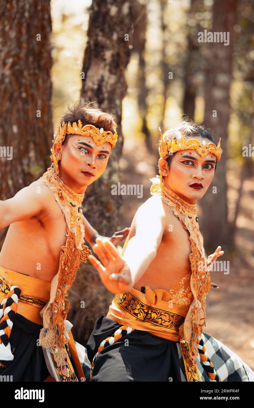 Two Balinese men dancing together in front of the tree while wearing a ...